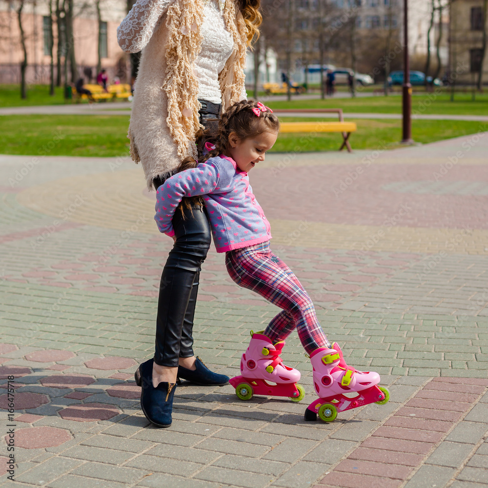 Mom and daughter ride on roller skates. Girl learning to roller skate ...