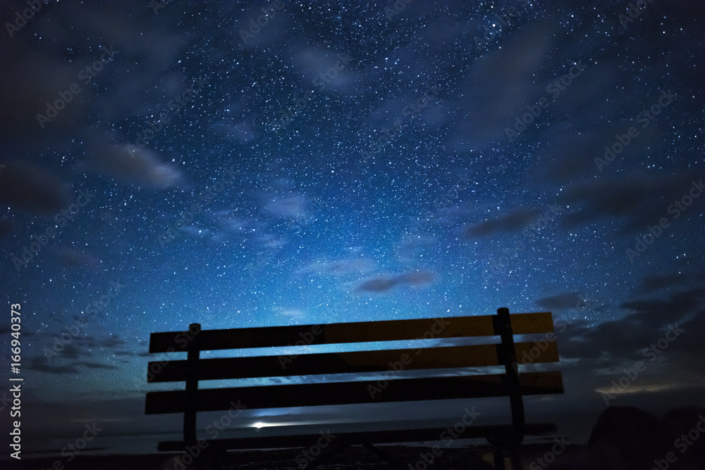 Wooden park bench silhouetted in front of view of night sky full of ...