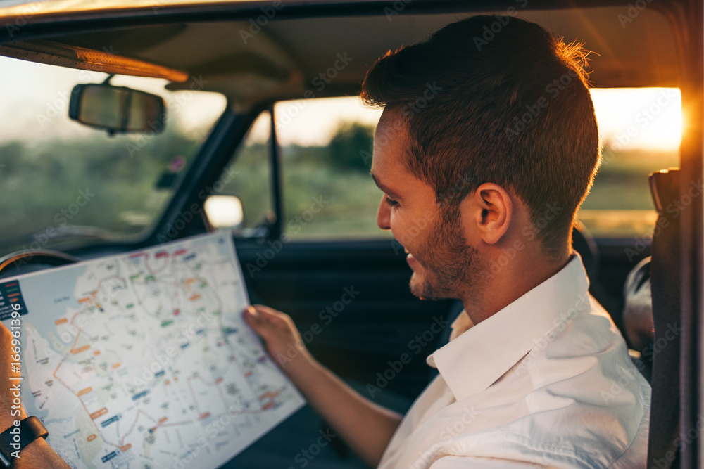 Side view of young smiling handsome man using a map on a roadtrip for ...