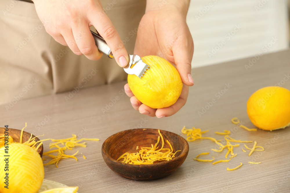 Woman taking off lemon peel with zester over table Stock Photo | Adobe ...