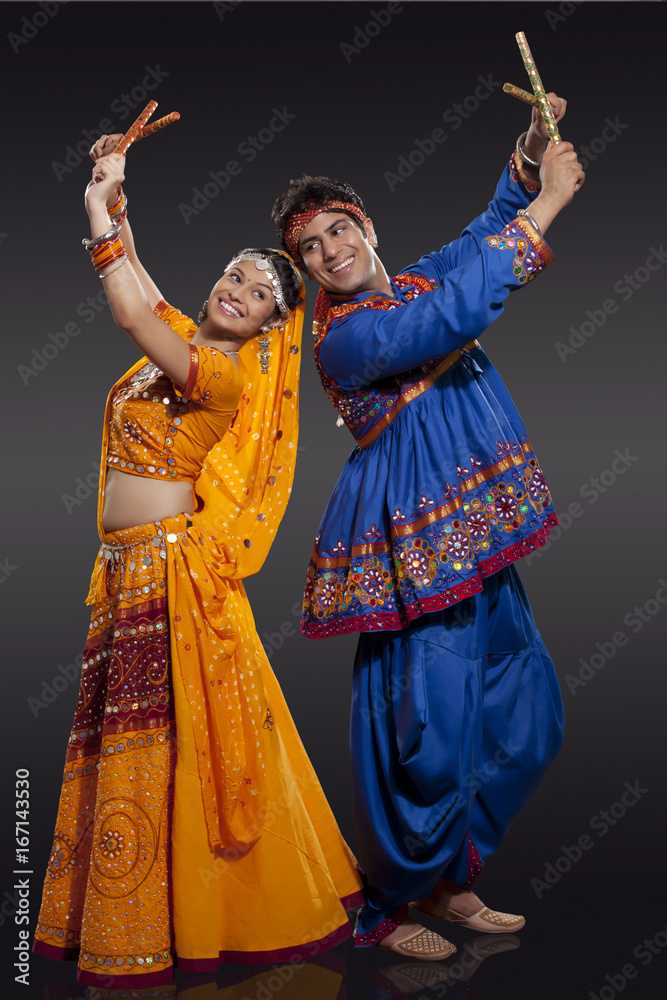 Happy young Indian couple performing Dandiya Raas over black background ...
