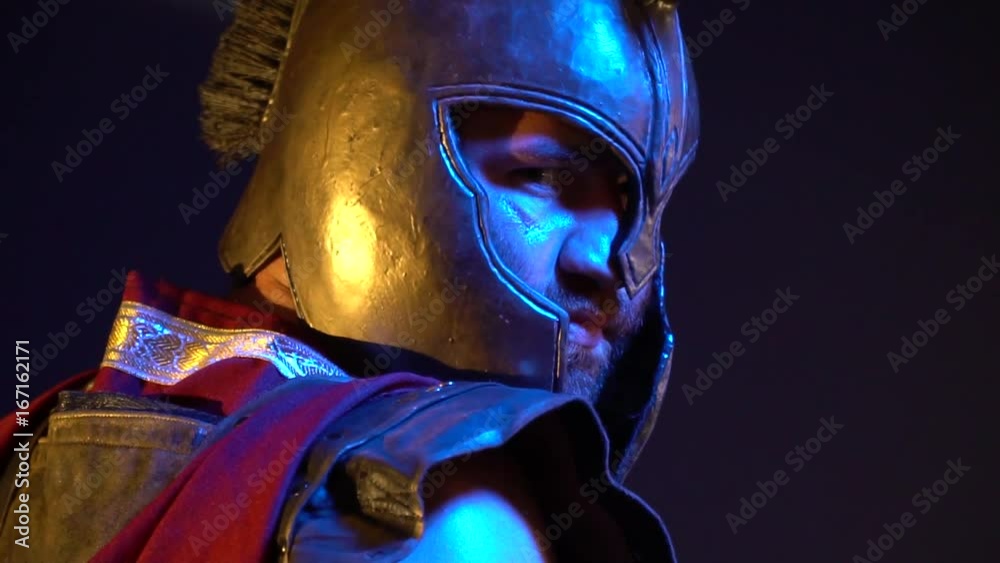 The gladiator in his helmet and red cloak is standing with his back and ...