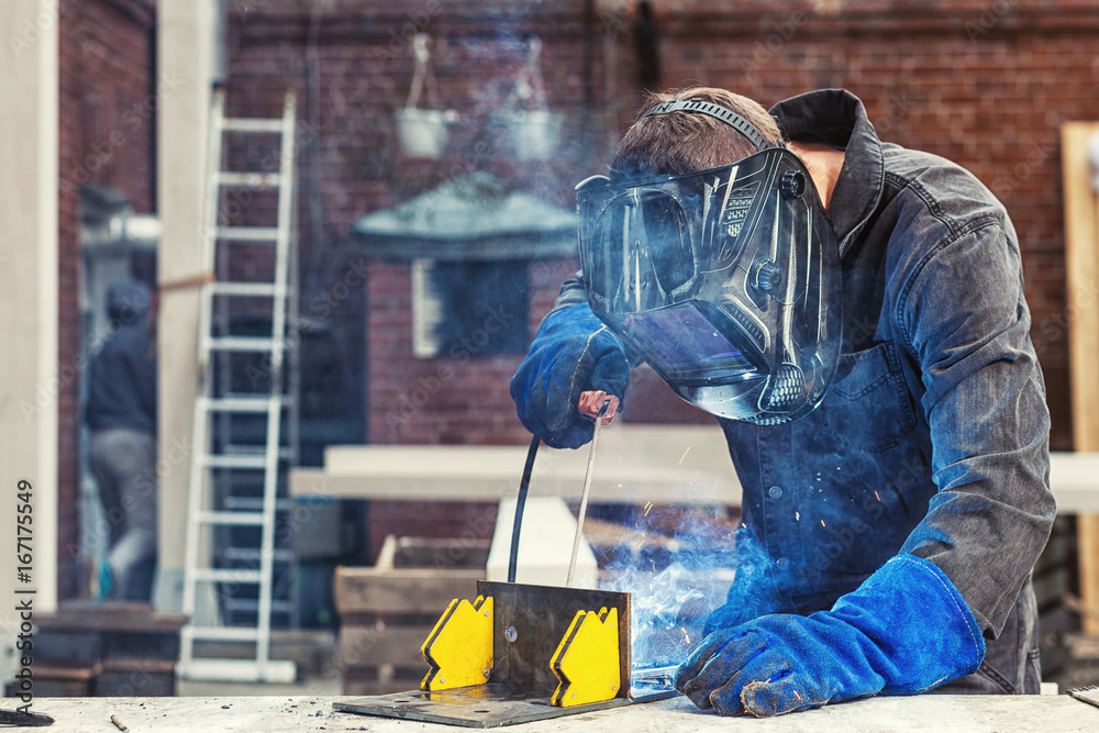 A strong man welder in a construction black overall and welding smear ...