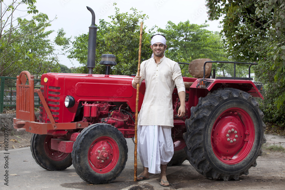 Portrait of a farmer with a stick standing next to tractor Stock Photo ...