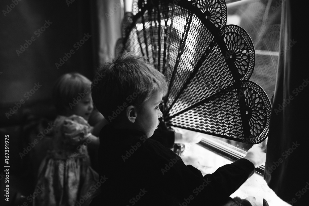 Two children look out of a window covered with an old fashioned screen ...