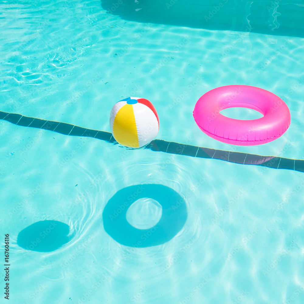 Poster Bright pink float and beach balls in blue swimming pool ...
