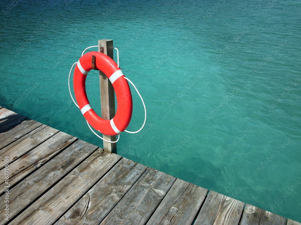 Leuchtend roter Rettungsring vor turkisgrünem Wasser im Sommer bei ...