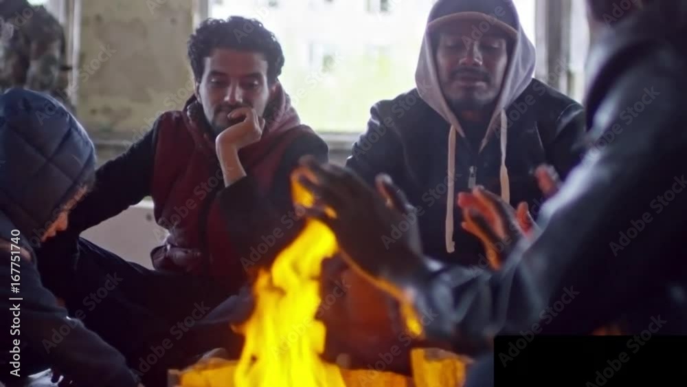 PAN of homeless Arab men and little boy sitting and warming their hands ...