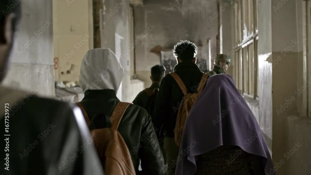 Tracking with rear view of male Arab refugees walking along hallway of ...