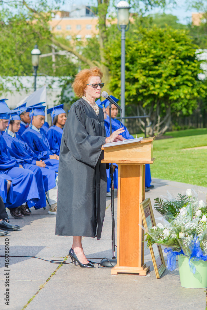 Principle standing at podium, giving speech, on graduation day ...