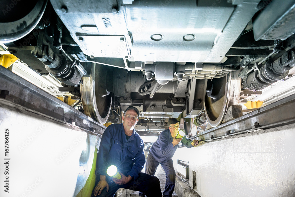 Locomotive engineers inspecting underside of locomotive in train works ...