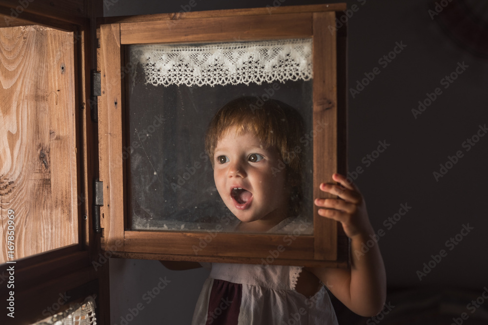 Surprised little girl looking through the window Stock Photo | Adobe Stock