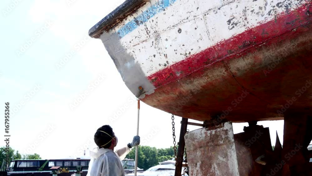 Worker covers metal with a primer paint of old rusty ship at shipyard ...