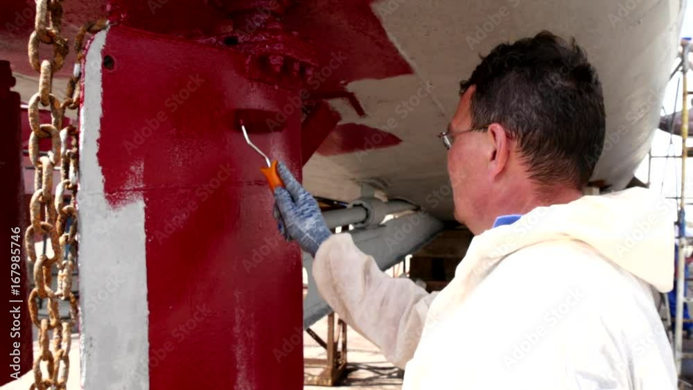 Worker paints metal of ship propeller red color at shipyard in port of ...