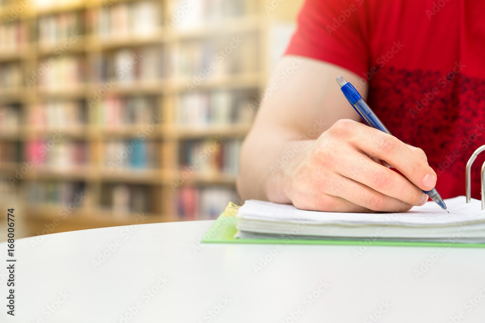 Young athletic man and student studying and writing notes in public or ...