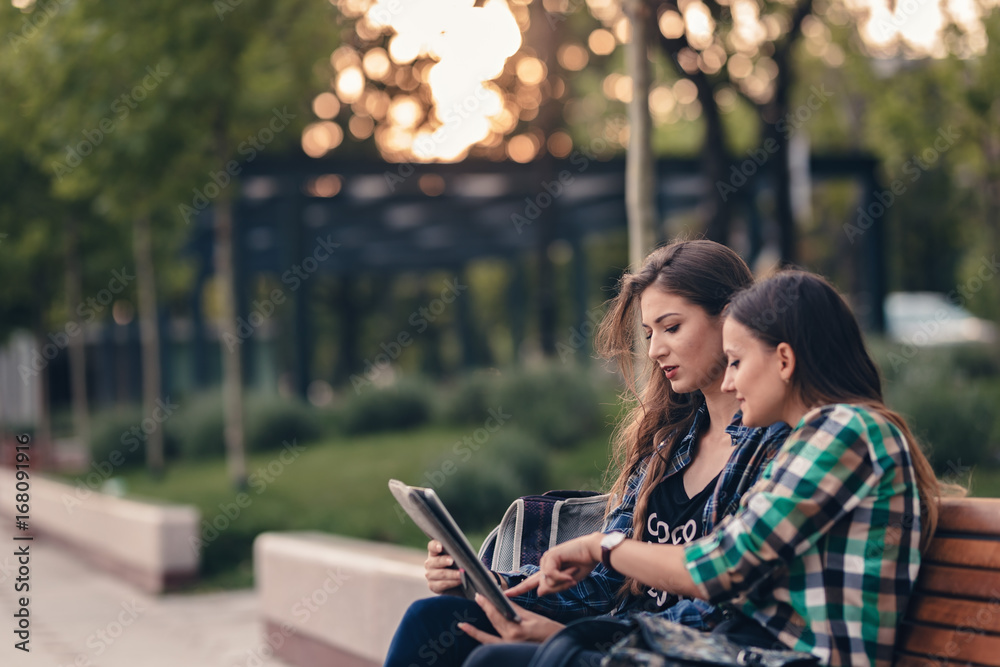 Stylish girls sitting on a bench in the park. Confused faces while ...
