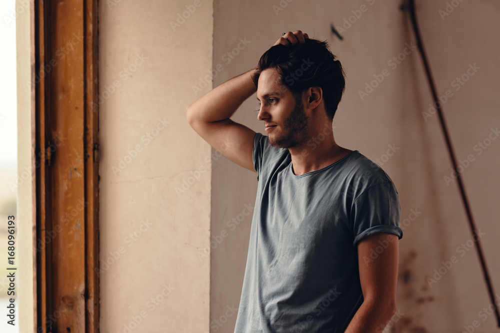 Fallen in deep thoughts, handsome guy standing near window and looking ...