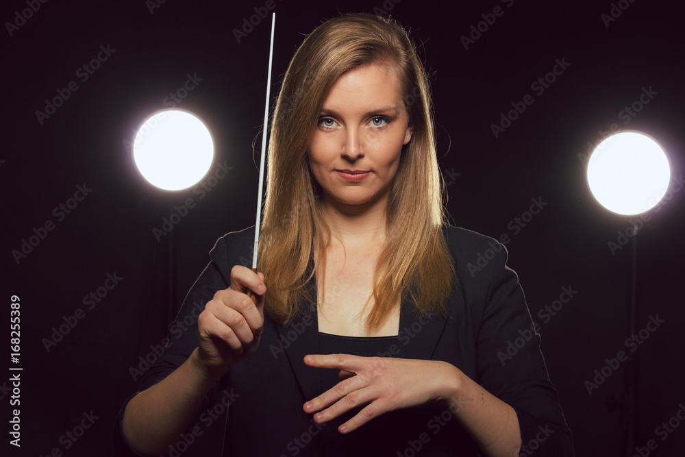 Young caucasian woman conductor poses with baton in a dark space with ...