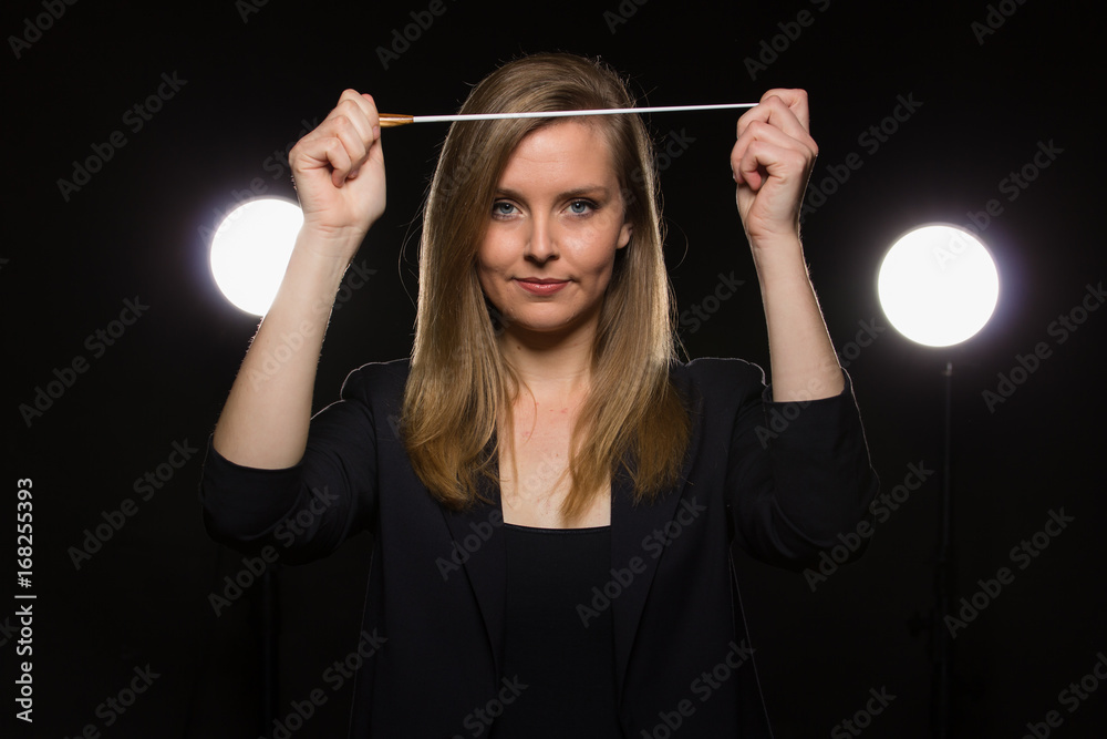 Young caucasian woman conductor poses with baton in a dark space with ...