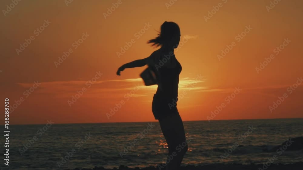 A young sexy girl woman is whirling at sunset or at dawn counter-clockwise with a straw hat in ...