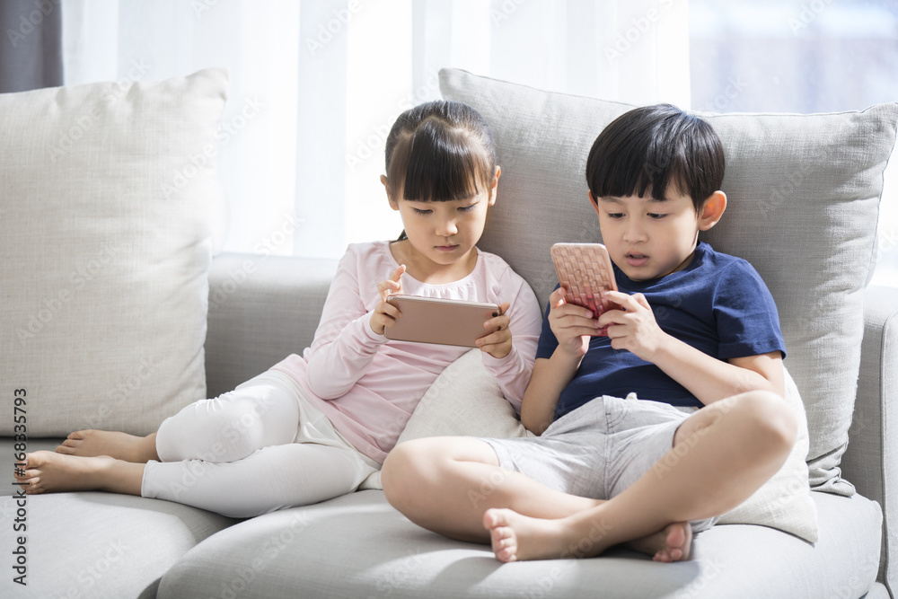 Happy boy and girl playing smart phones in sofa Stock Photo | Adobe Stock