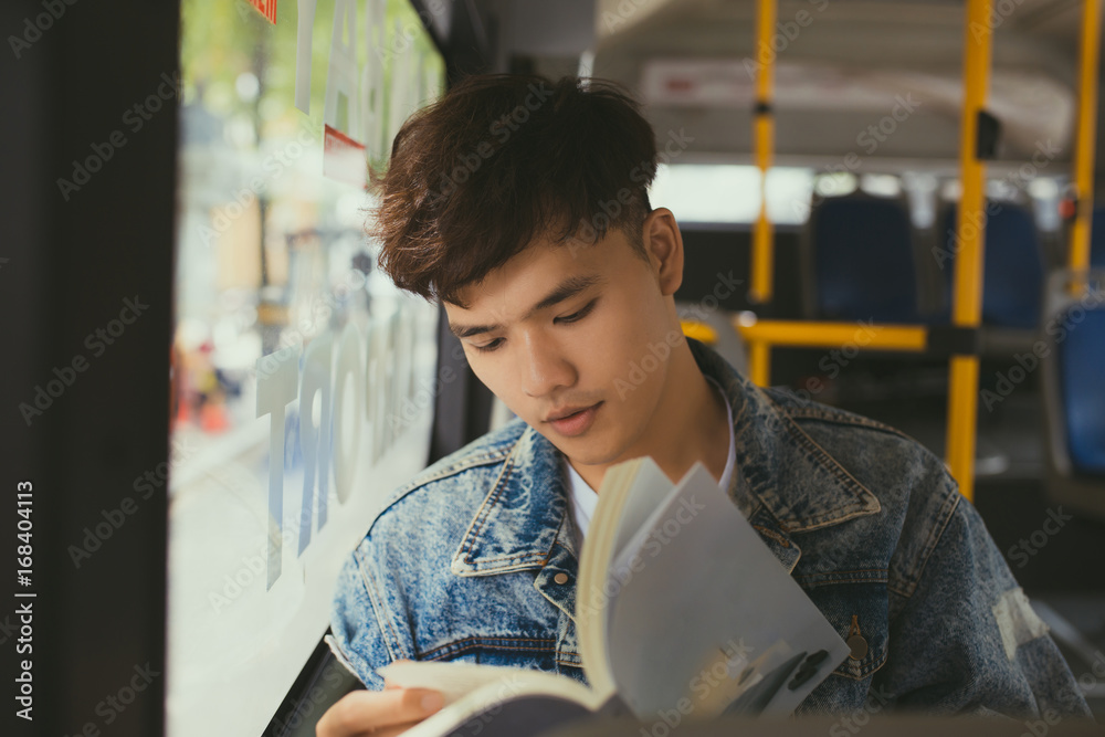 Young man sitting in city bus and reading a book. Stock Photo | Adobe Stock
