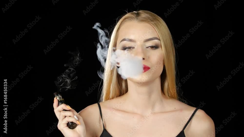Girl smokes an electronic cigarette in a dark room. Black background ...
