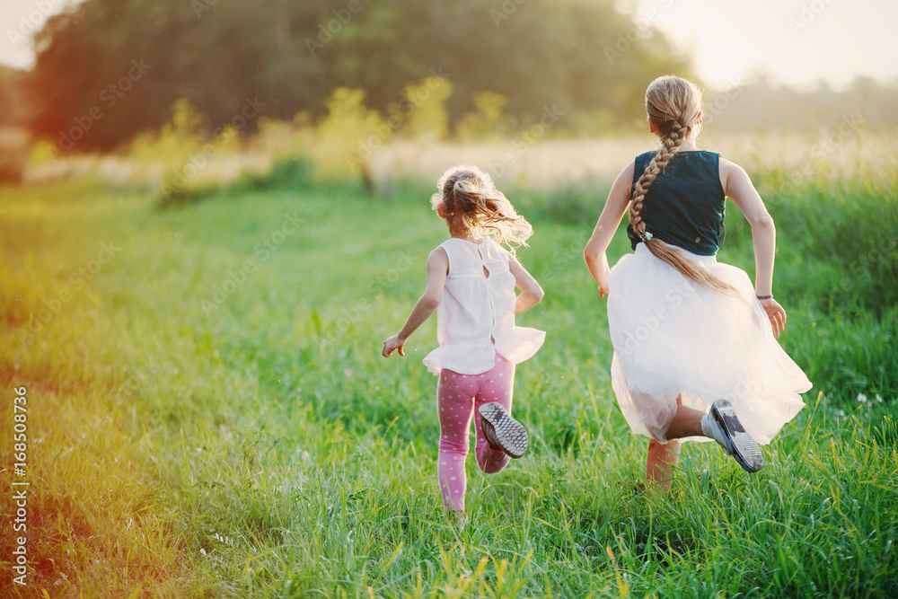 Two little girls having fun running on the field. Sisters are playing ...