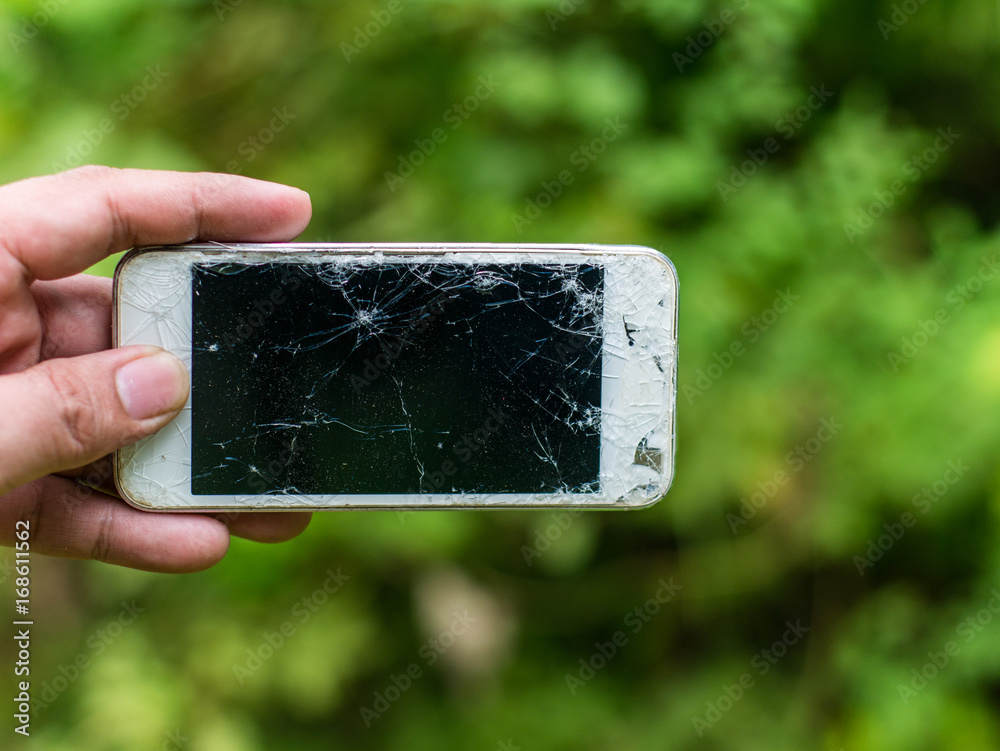 Man's hand holding a broken mobile phone with green nature background ...