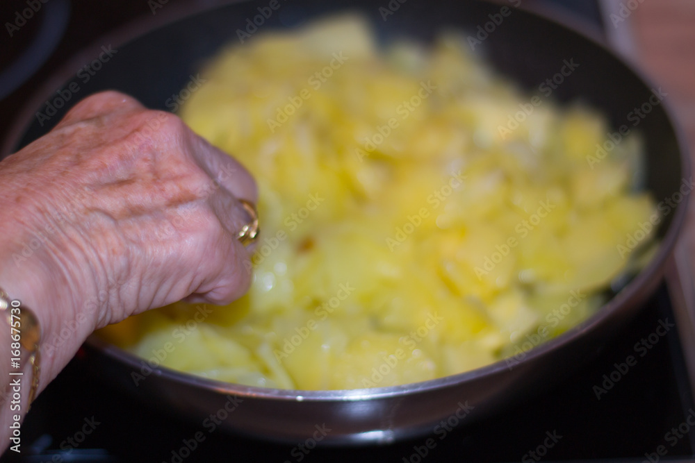 Old woman cooking traditional Spanish omelette. Cooking potatoes in a ...