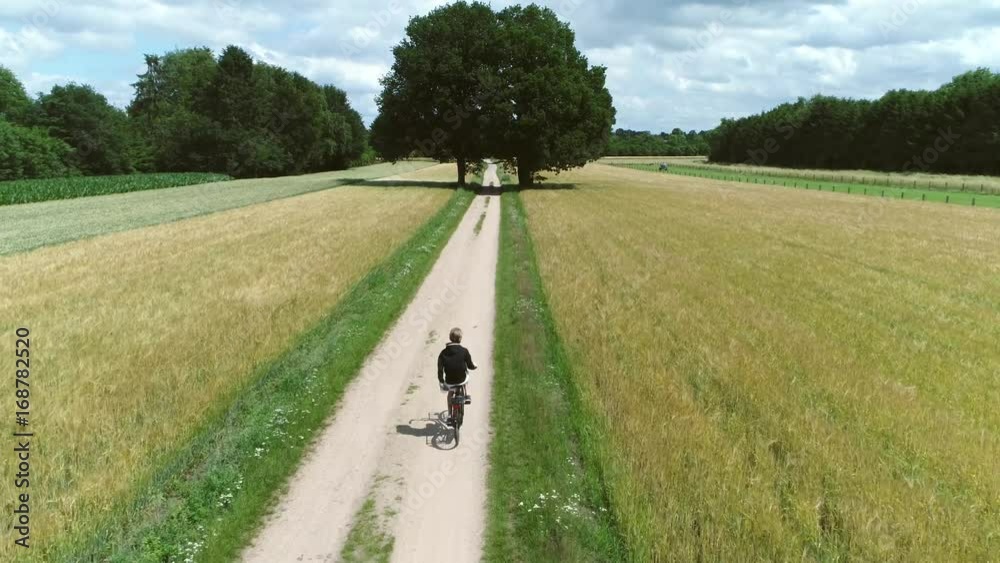 Aerial flying in rural area above bike path then cyclist drives past ...