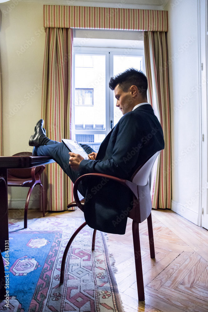 Side view of elegant businessman sitting on chair putting legs on table ...