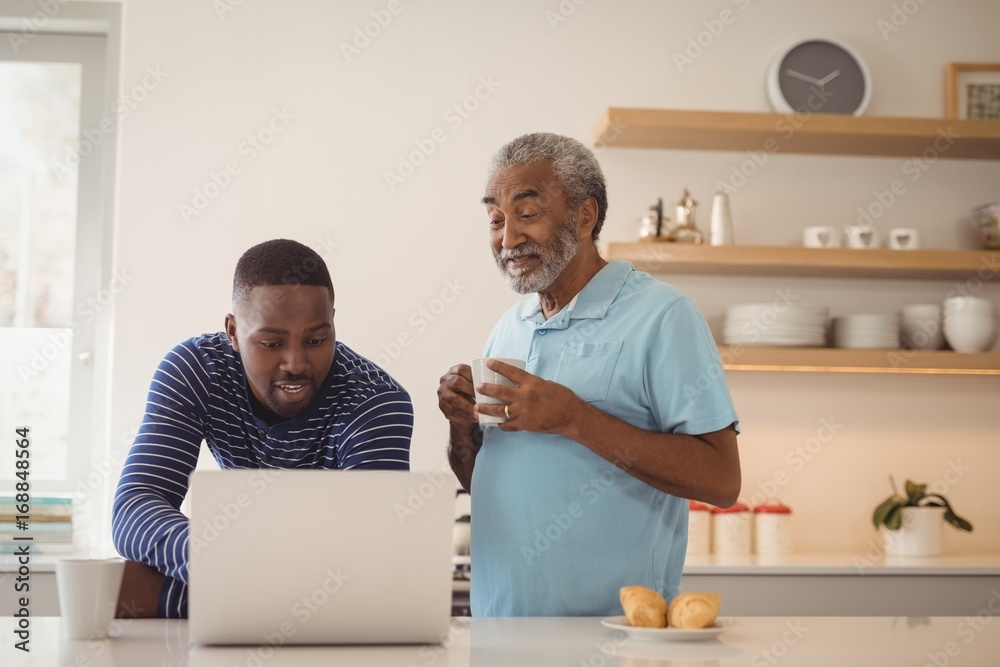 Father and son using laptop while having coffee in kitchen Stock Photo ...