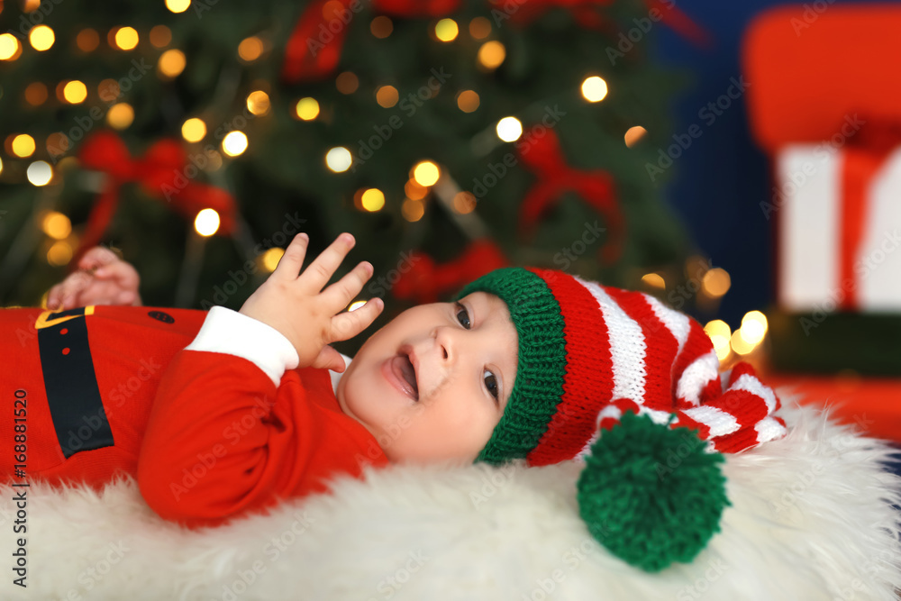 Cute little baby in Santa costume lying against blurred Christmas ...