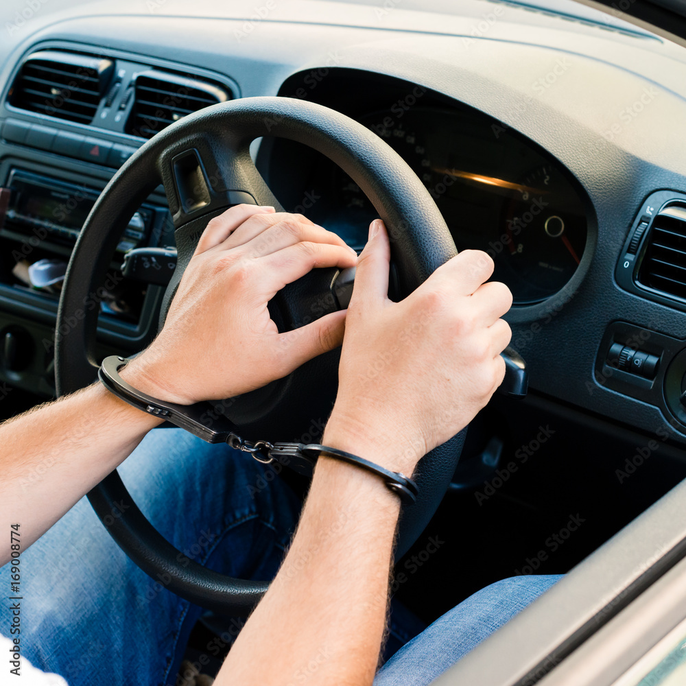 handcuffed hands of an offender sitting behind the wheel of a car ...