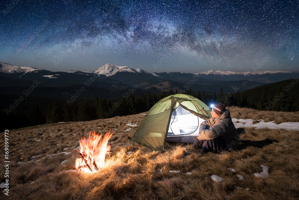 Male tourist enjoying in his camp at night. Man with a headlamp sitting ...
