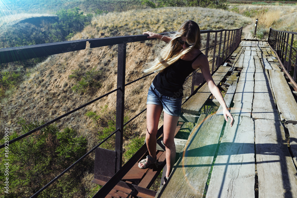 Beautiful young girl falls through the old rustic bridge. Actively ...