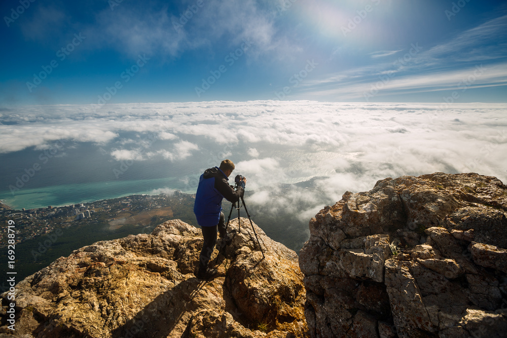 Man standing with a tripod and camera on a high mountain peak above ...