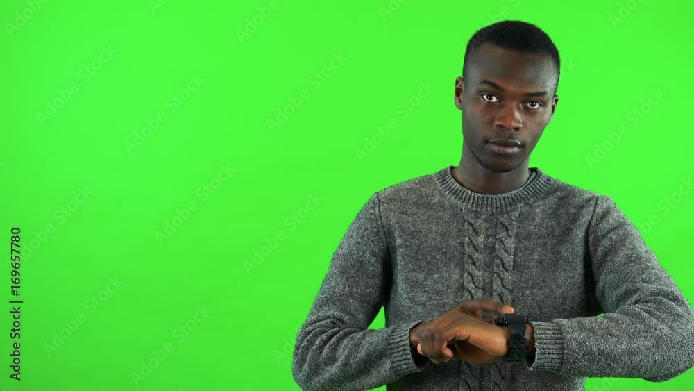 A young black man looks at the camera and taps the watch on his wrist ...