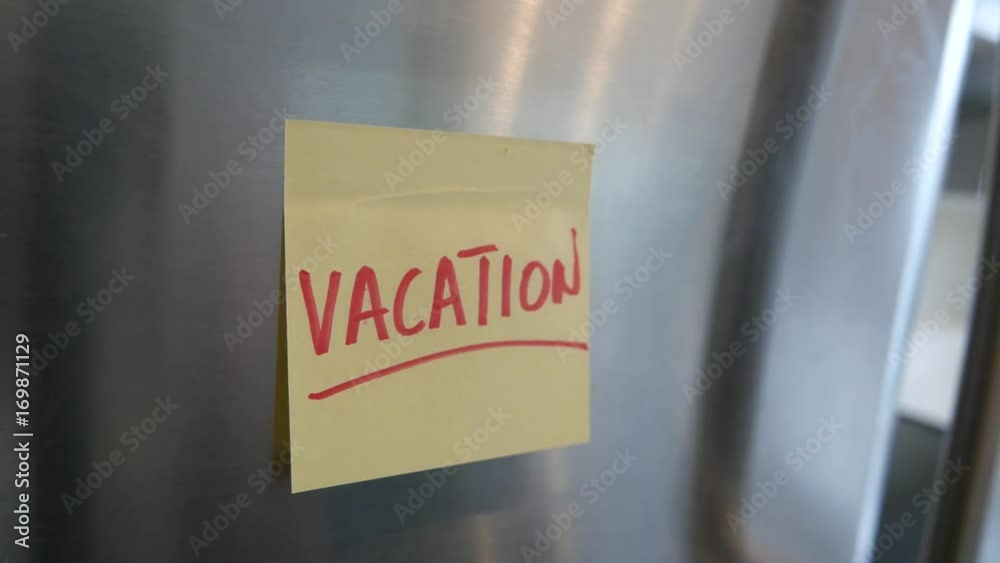 Putting a Vacation sticky note reminder on a fridge. Closeup on the ...
