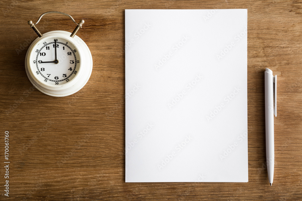 White paper with pen and clock on the wooden table. Examination time ...