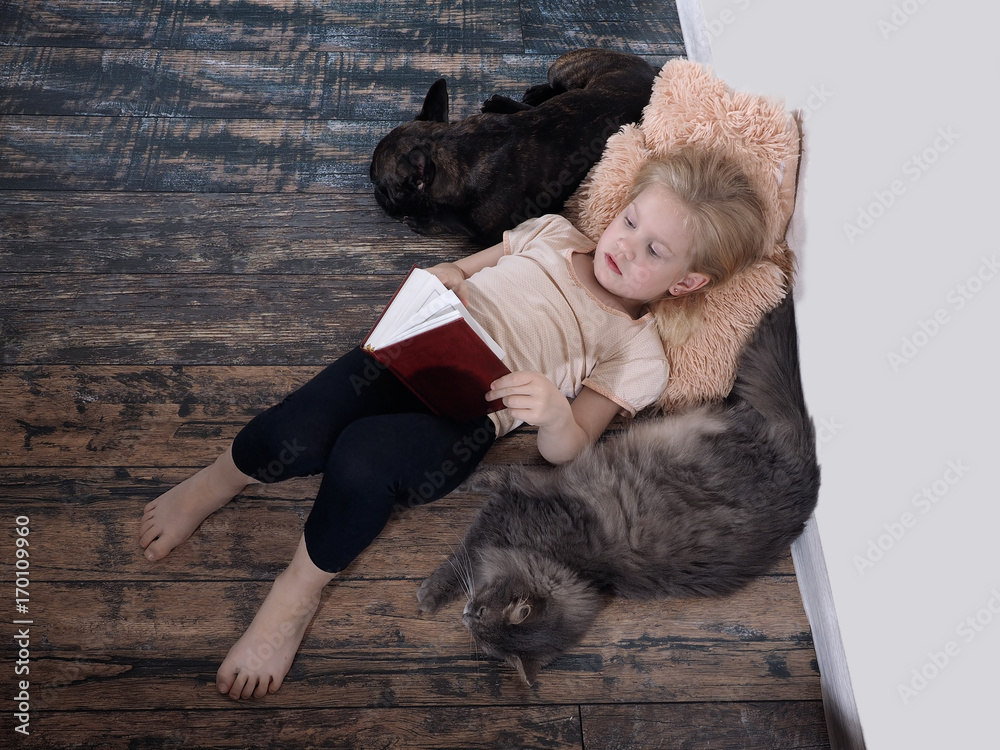 small child with a book. Girl lying on the floor. Next a cat and a dog ...