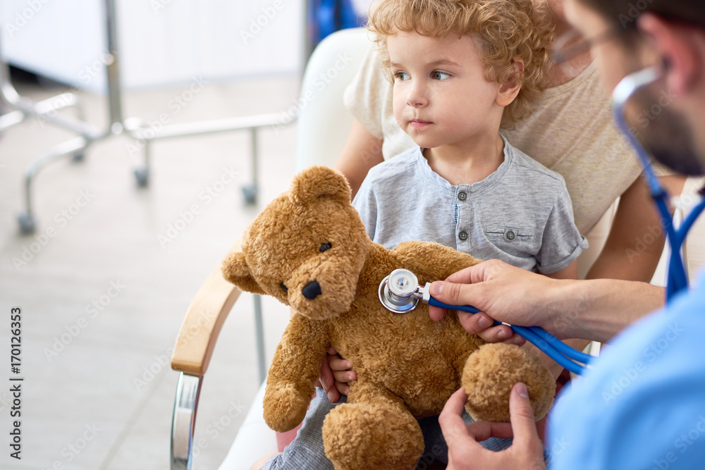 Portrait of adorable curly child in doctors office holding teddy bear ...