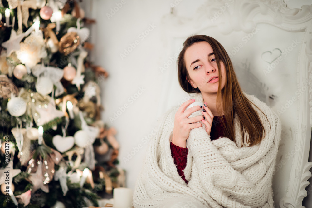 Young woman relaxing with a mug of coffee as she cuddles up in warm ...