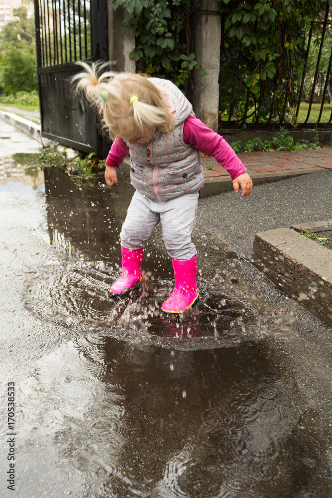 Foto de Little girl jumping in the mud in a puddle, splashing water. do ...