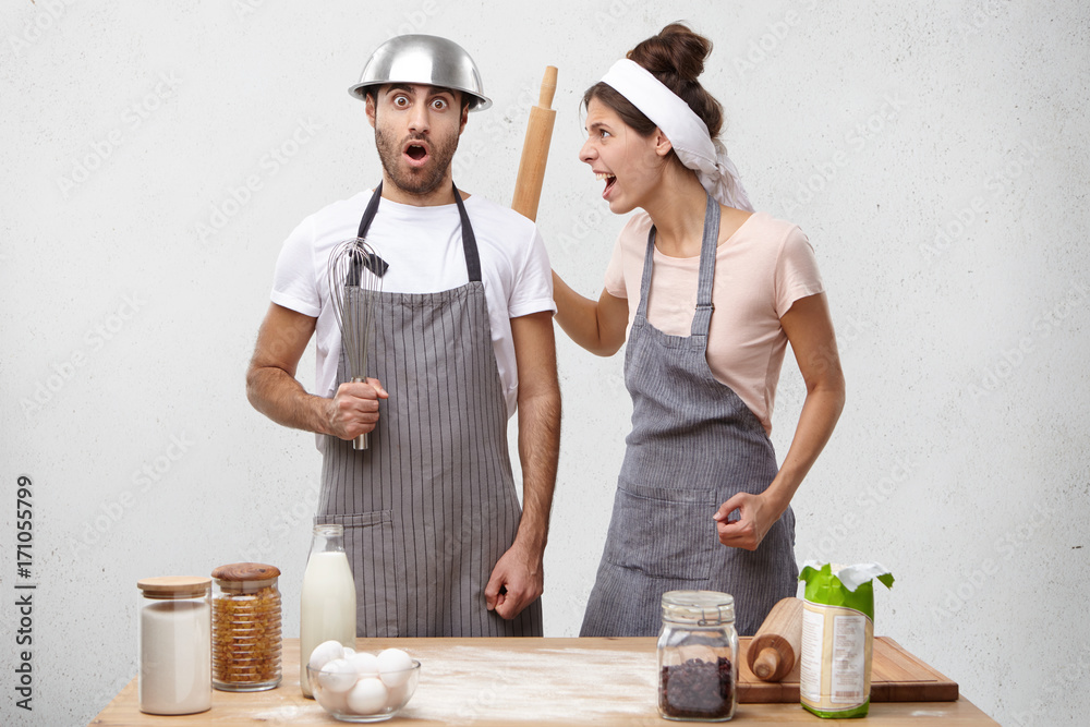 Furious housewife wearing apron, raising her hand with rolling pin ...
