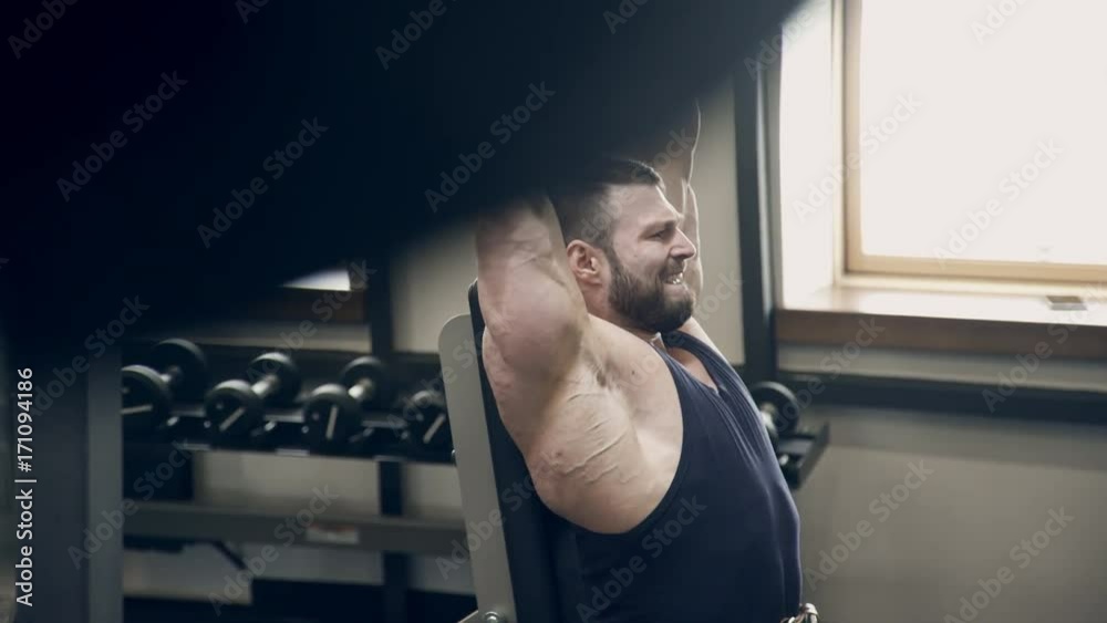 Bodybuilder with a beard carefully lifts a dumbbell hands up. Brutal ...
