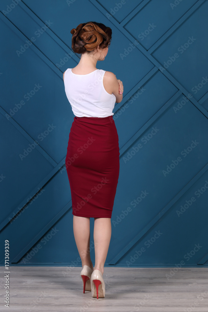 Beautiful woman with hairdo and in skirt poses in blue studio, back ...