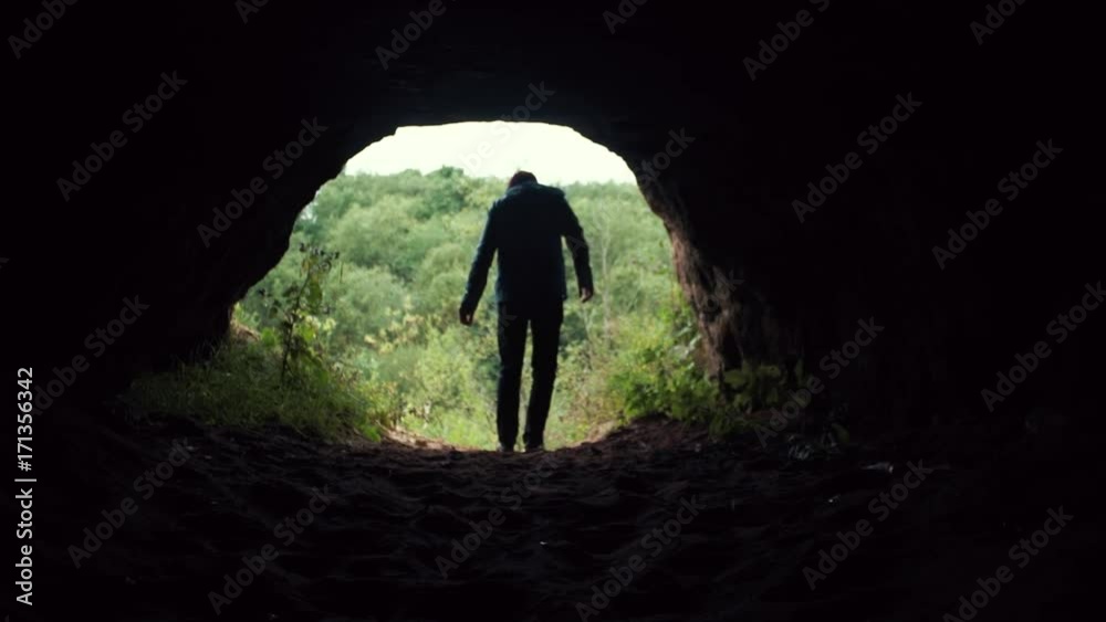 Young hiker exits from dark cave chamber from darkness to day light ...