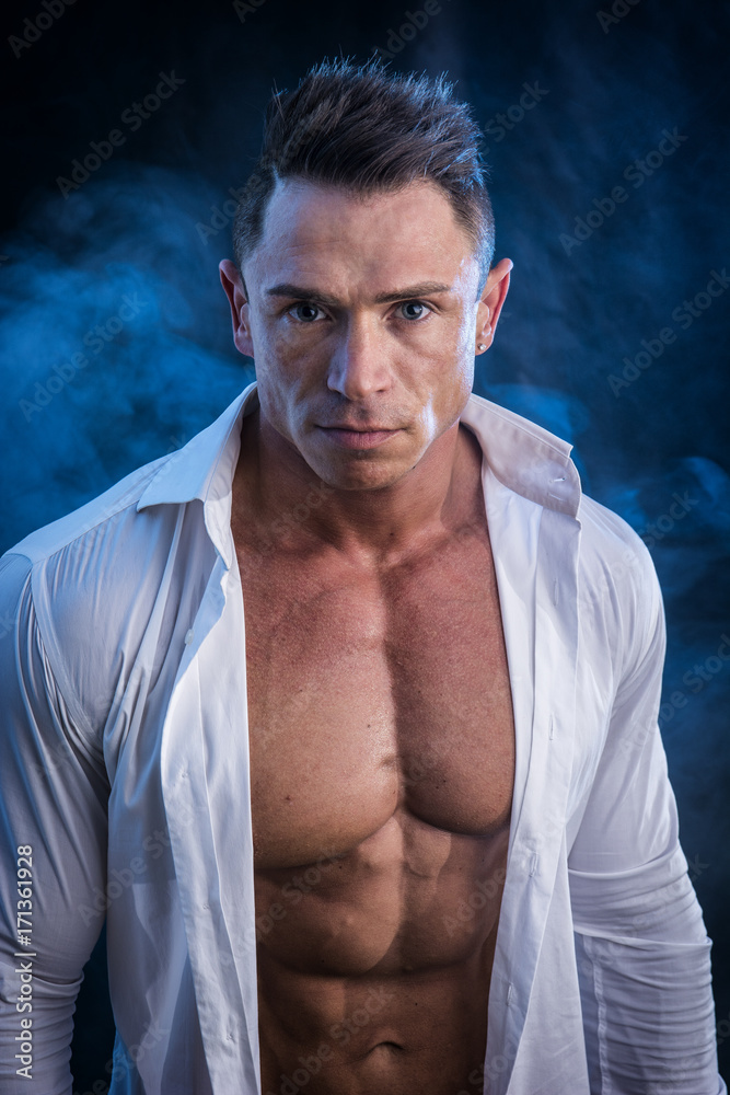 Male bodybuilder opening his shirt revealing muscular torso, on black ...